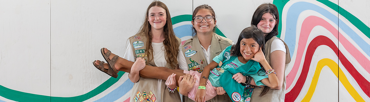 group of girl scouts smiling at each other wearing uniform vests.